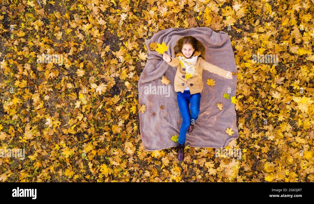Nice girl lying on back surrounded by autumn leaves, view from above ...