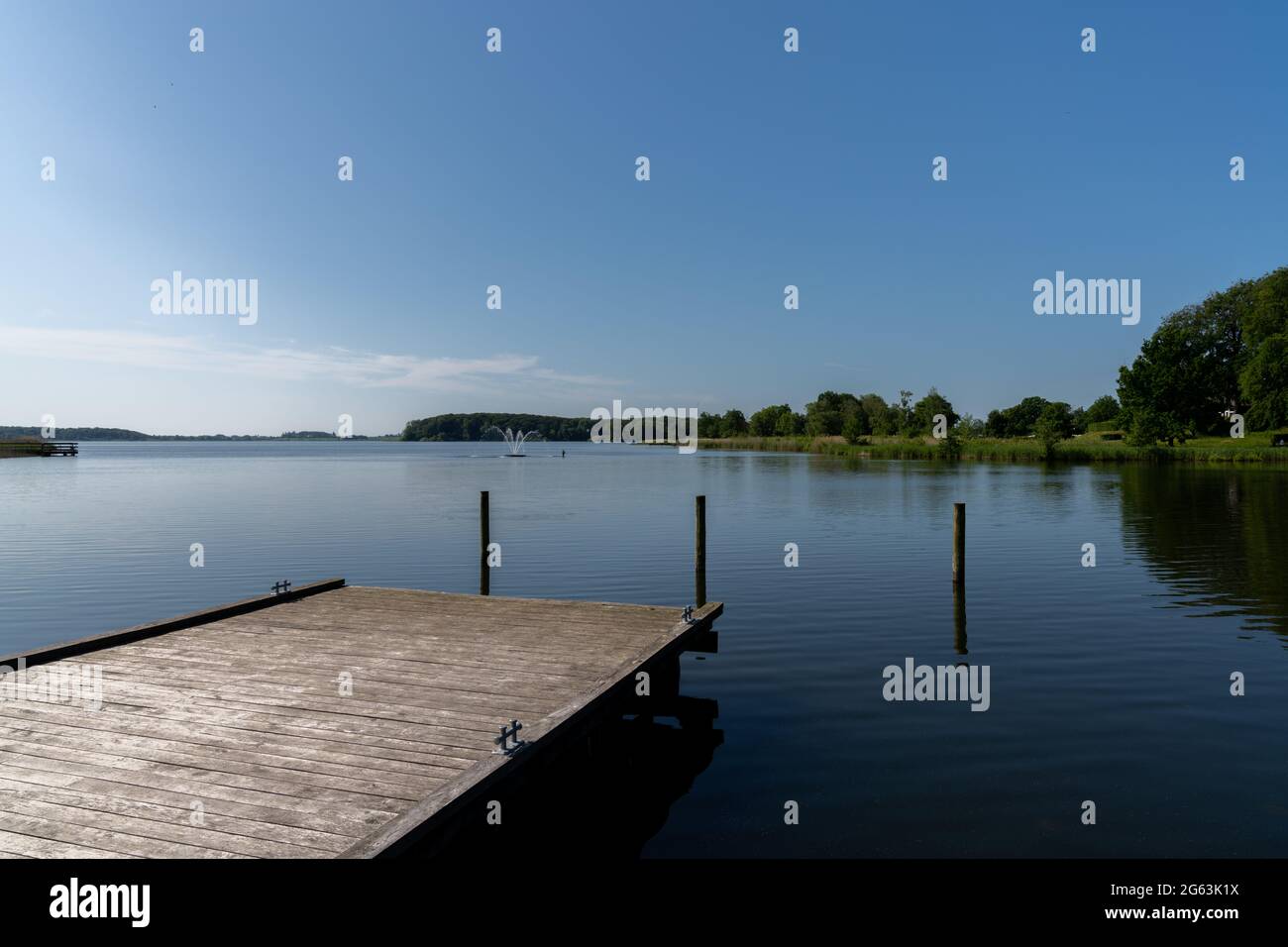 A wooden dock leads out into a calm lake with dark blue water Stock ...