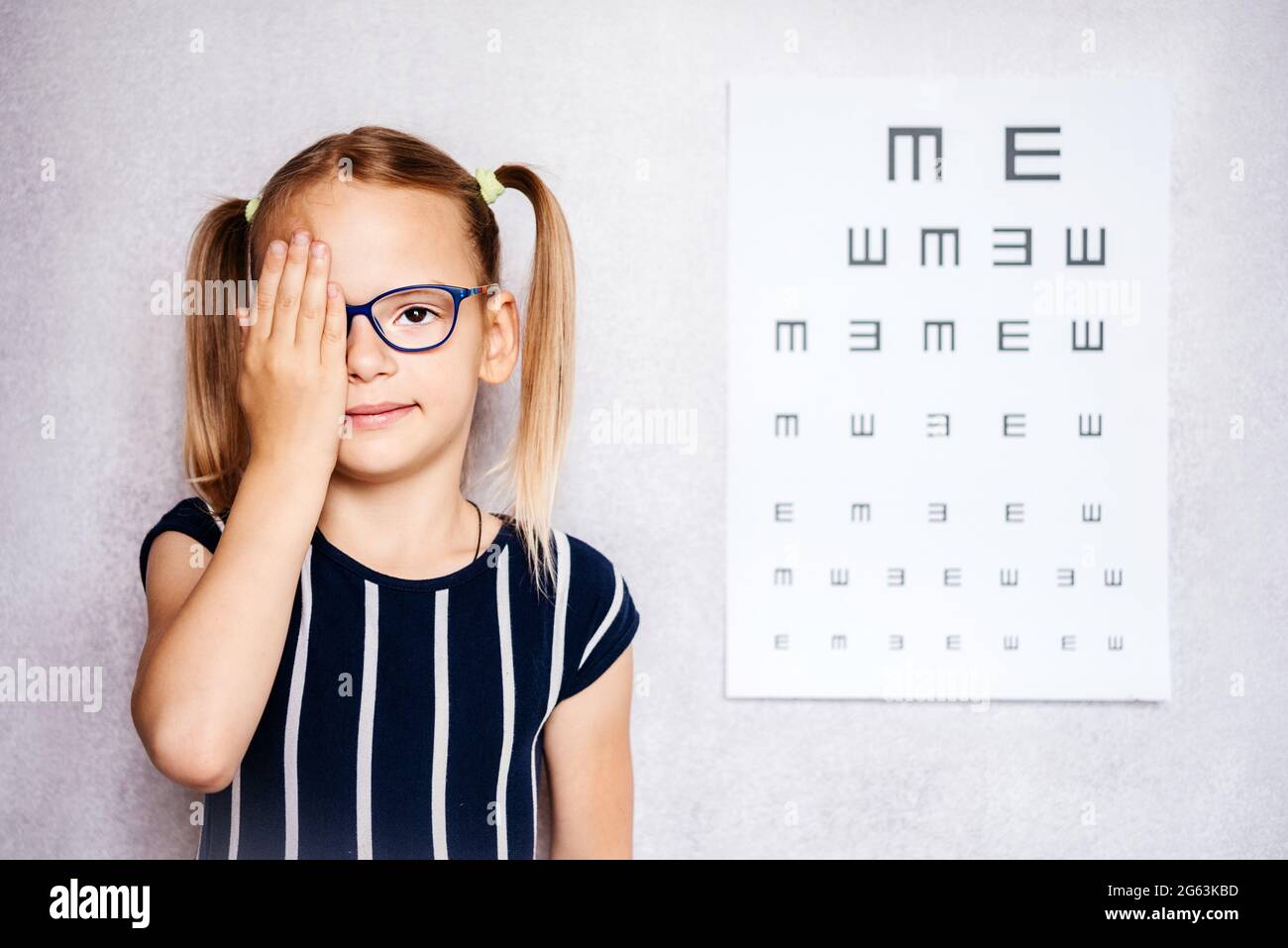 Little girl wearing eyeglasses taking eyesight test before school with ...
