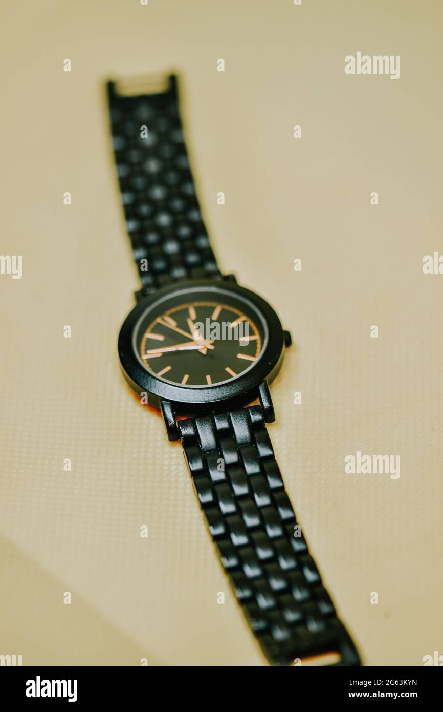 Vertical shot of black wristwatch isolated on a cream background with ...