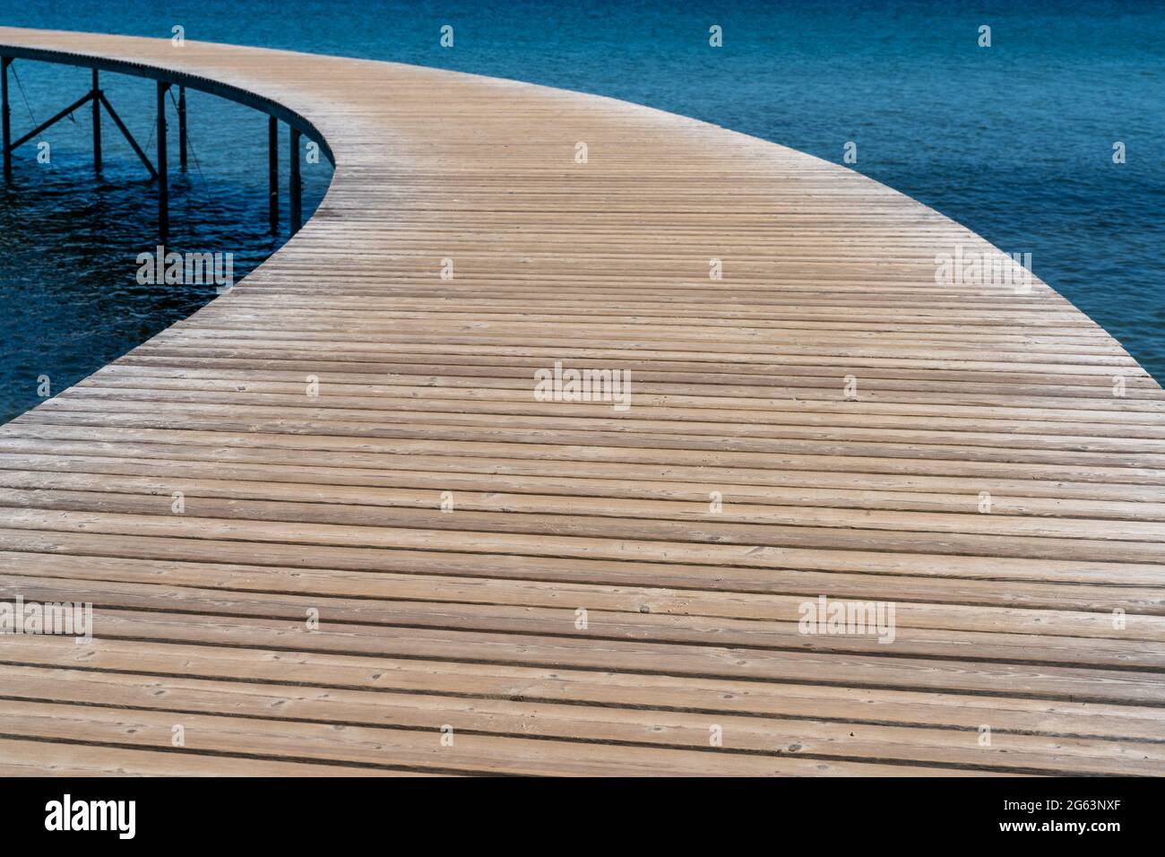A curved wooden boardwalk leads out into the blue ocean Stock Photo - Alamy