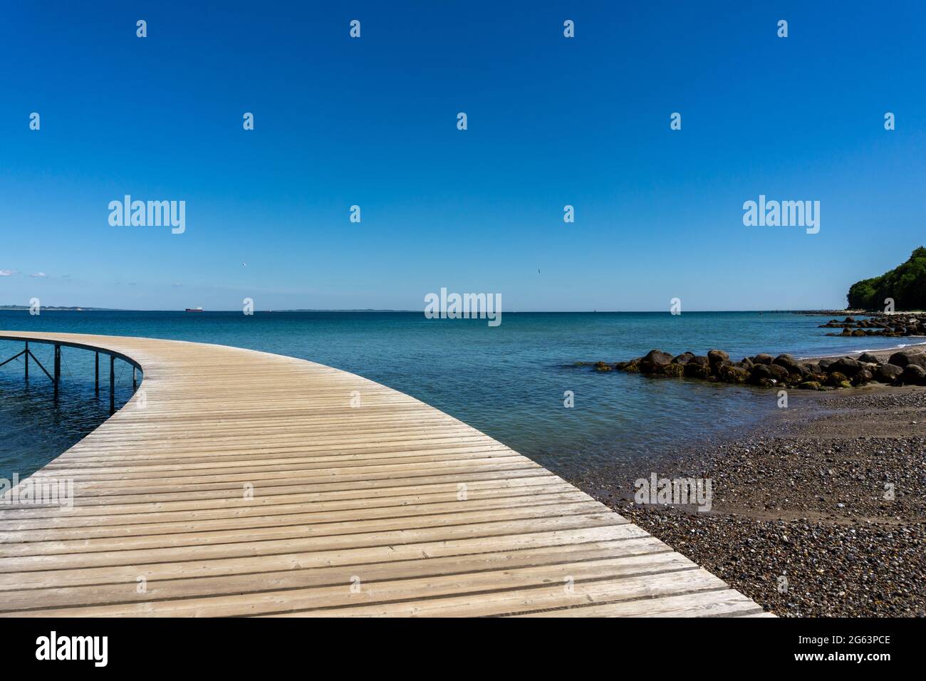 A curved wooden boardwalk leads out into the blue ocean Stock Photo - Alamy