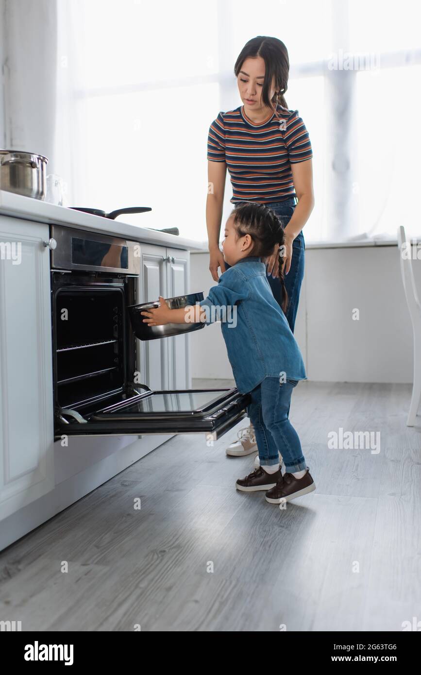 Asian kid putting pan in oven near mother in kitchen Stock Photo - Alamy