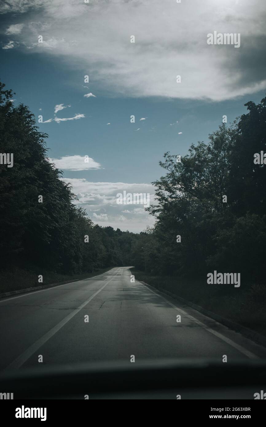 Dramatic shot of a road with trees on both sides seen through the front ...