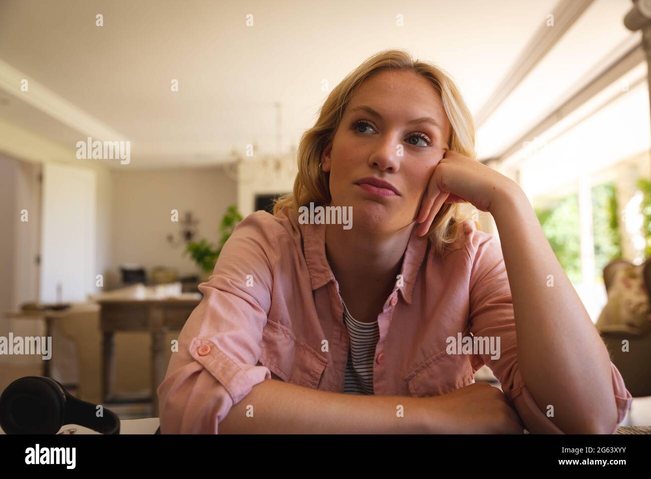 Caucasian woman sitting at table working in living room, leaning on ...