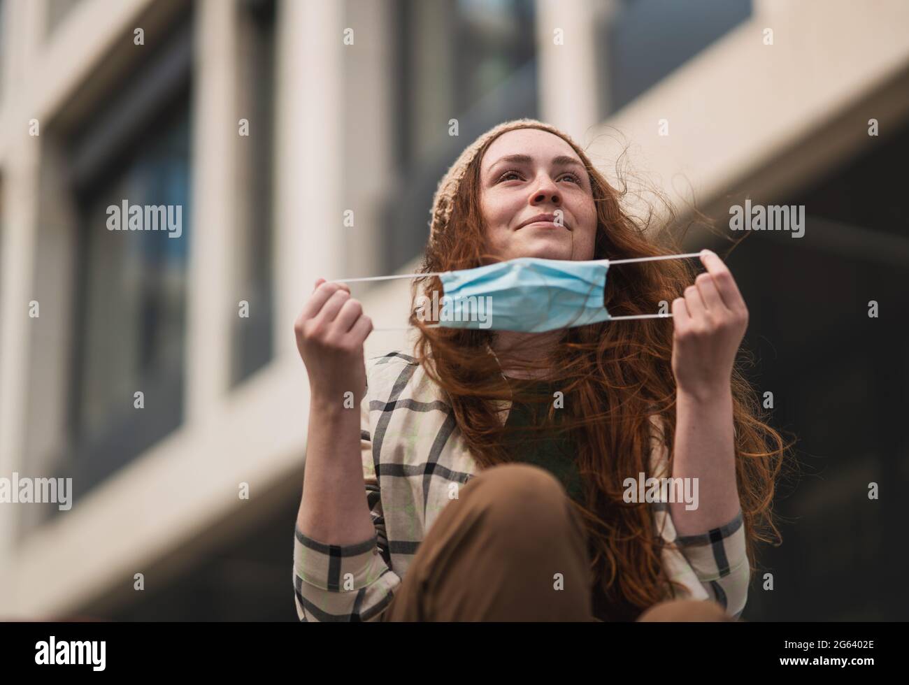Portrait of young woman taking off face mask outdoors in city, life ...