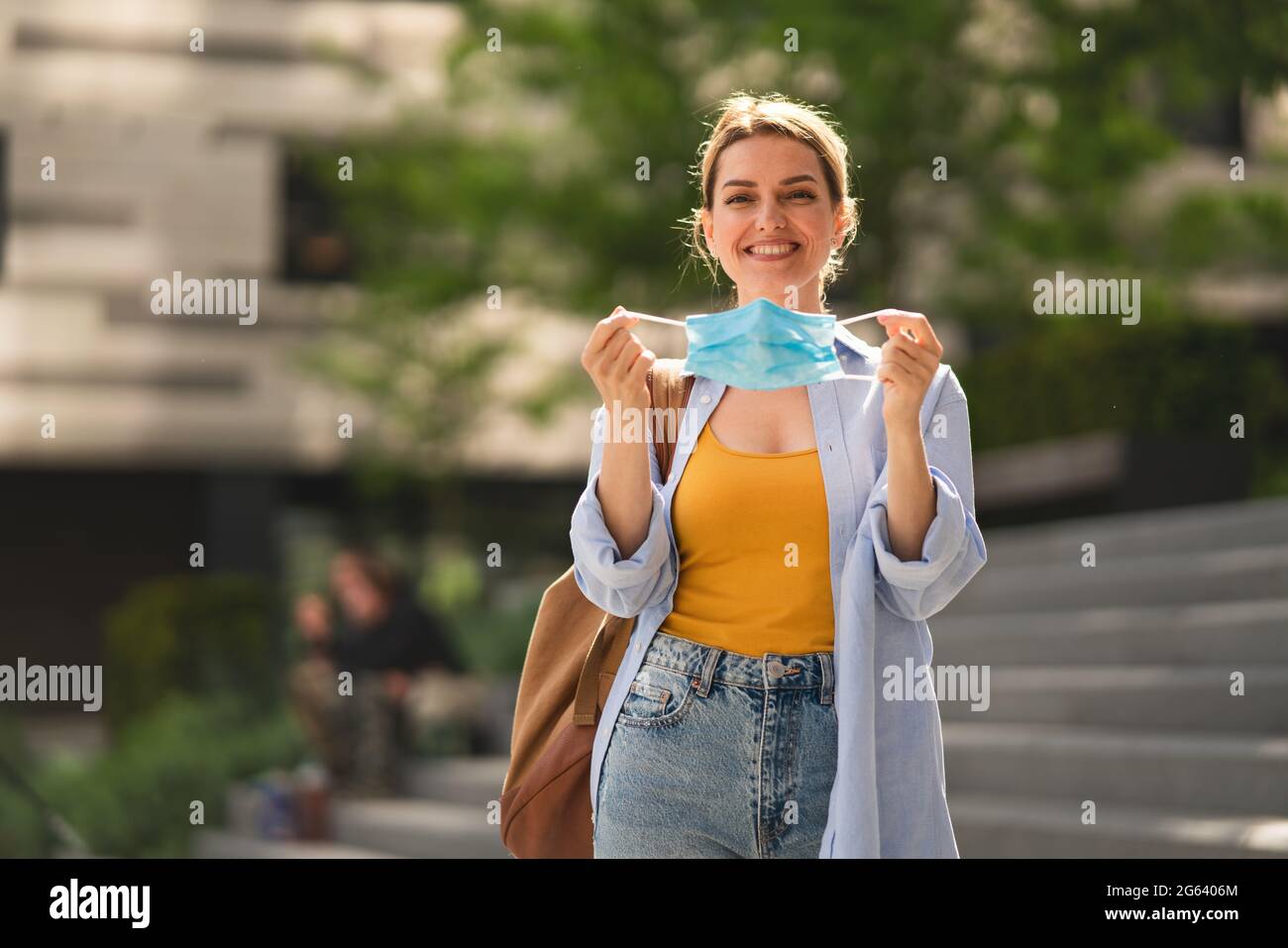 Portrait of young woman taking off face mask outdoors in city, life ...