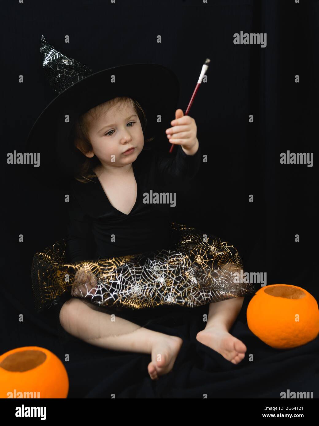 A little cheerful girl in a witch costume-a hat and a skirt with a ...