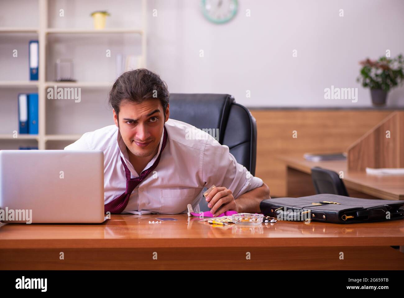Young drug addicted male employee sitting at workplace Stock Photo - Alamy