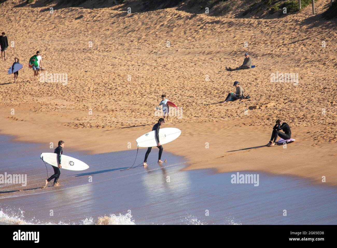 Australian male surfers carry their surfboards on Avalon Beach in ...