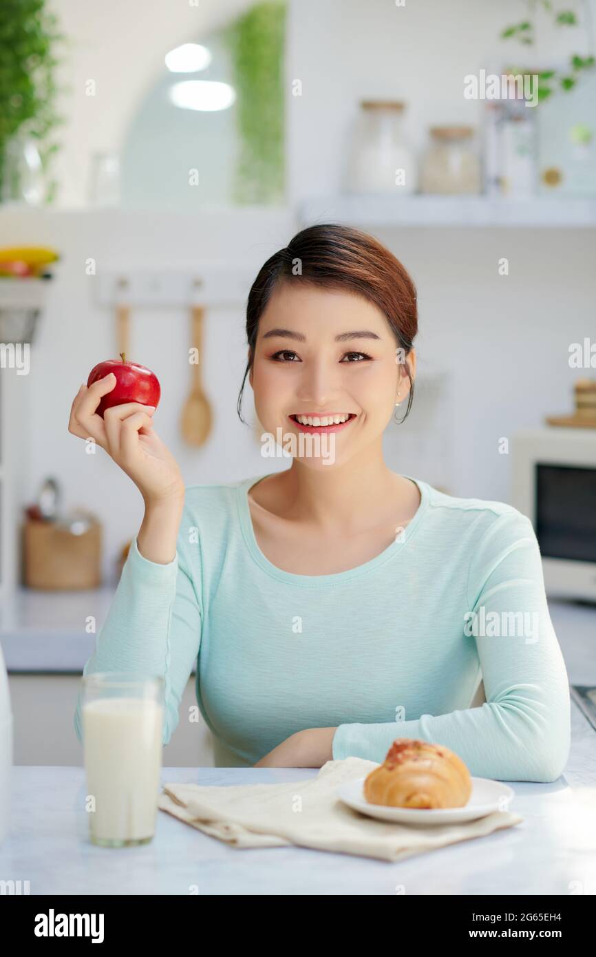 Girl sitting in kitchen on the desk with milk, apple and croissant ...