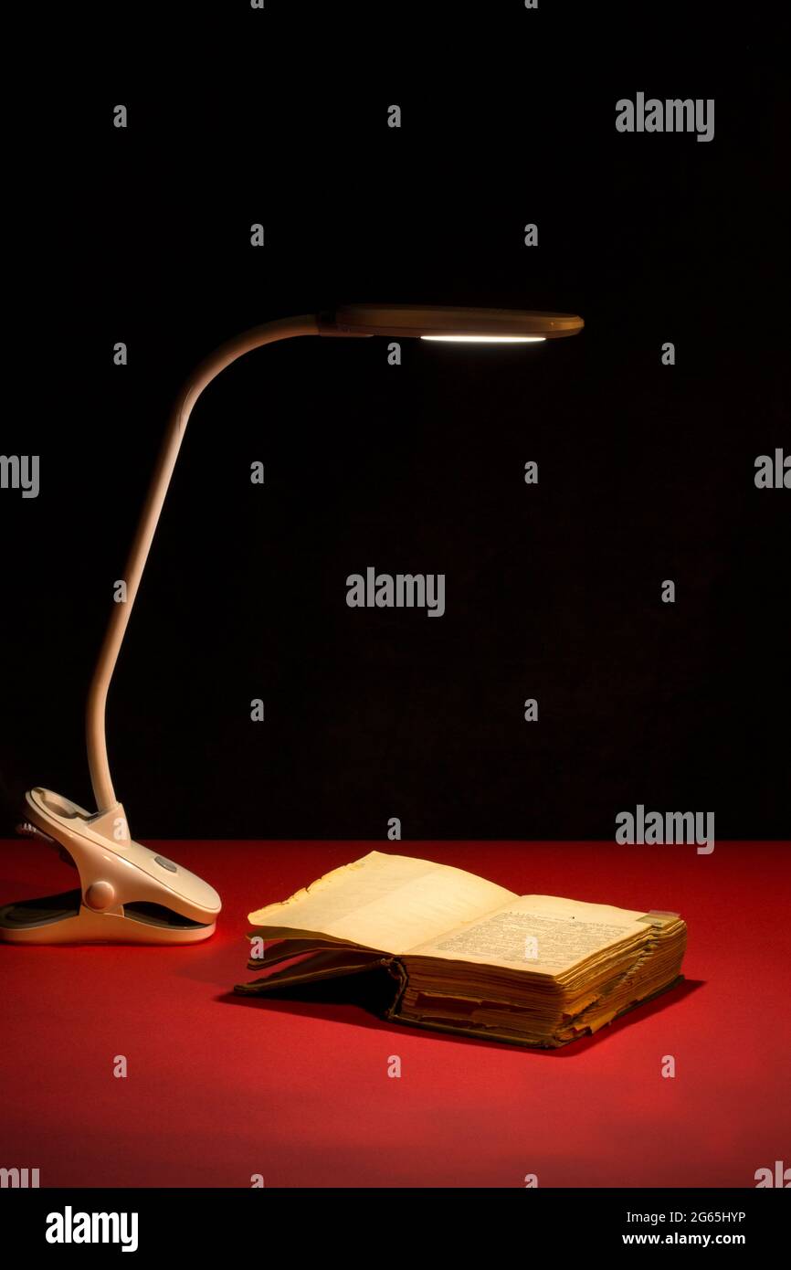 Table lamp illuminates an open book on a red table Stock Photo - Alamy