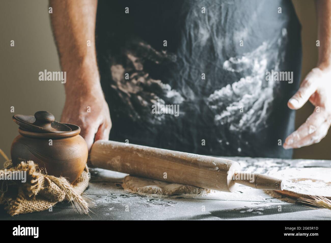 Male hands roll dough and flour with rolling pin next to clay pot and ...