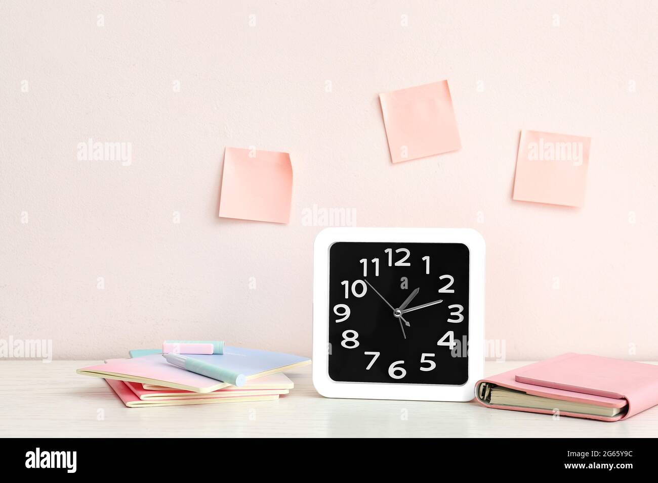 Stylish clock with notebooks on table near light wall Stock Photo - Alamy