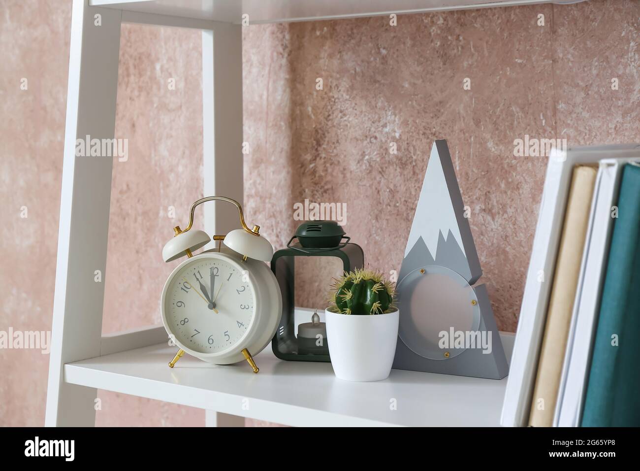Book shelf with alarm clock and decor near color wall Stock Photo - Alamy