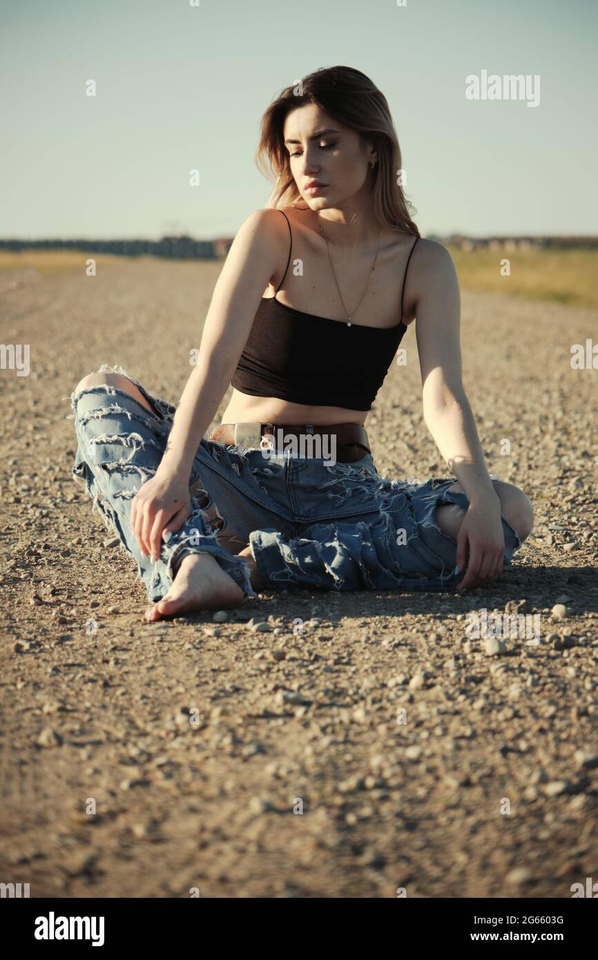serious sad tramp girl in torn jeans sits on a deserted road Stock ...