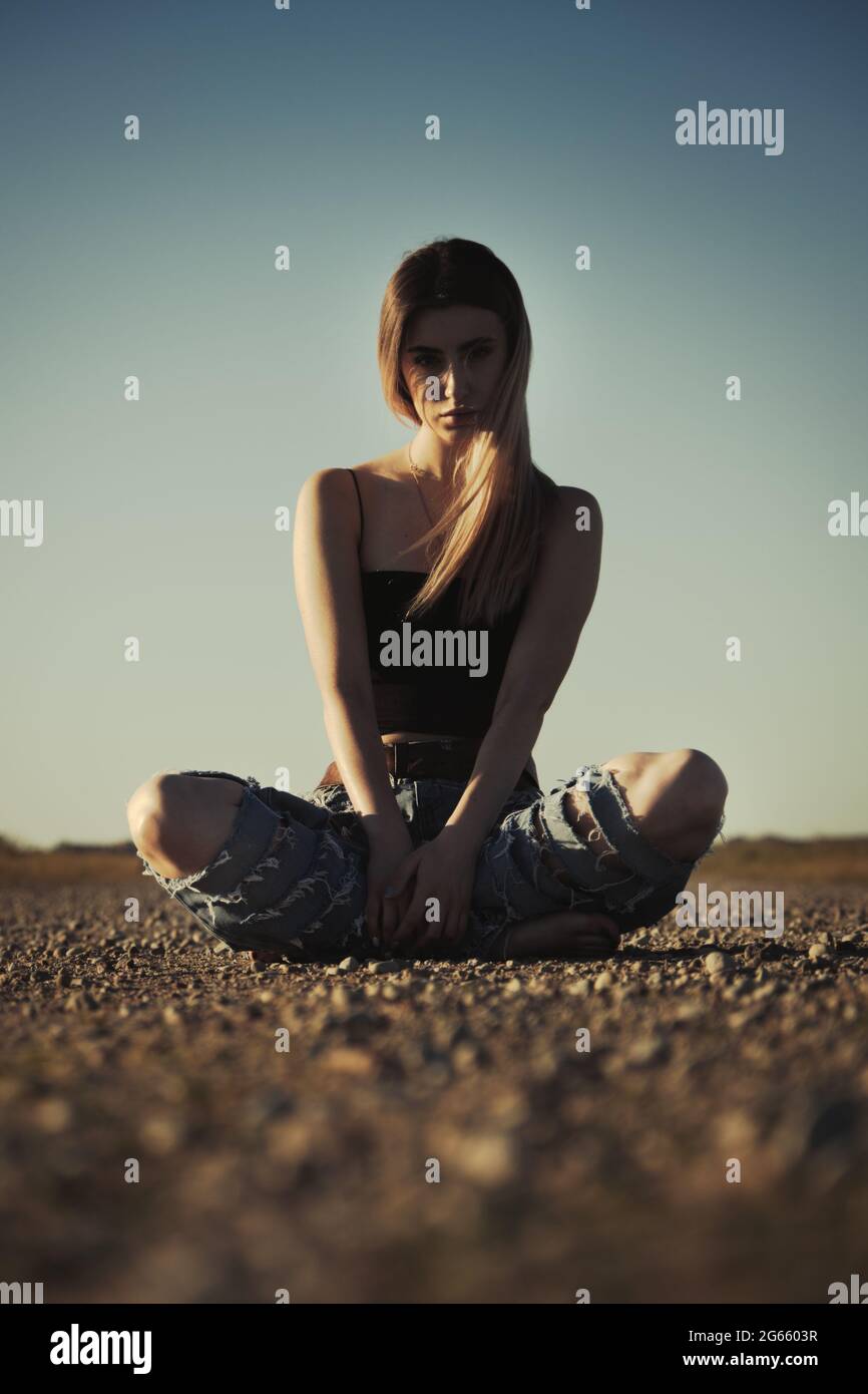serious sad tramp girl in torn jeans sits on a deserted road Stock ...