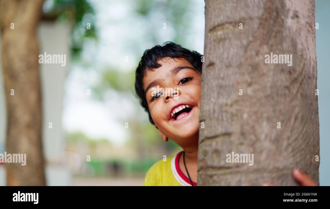 Little kid making fun behind the tree. Boy seeing someone behind the ...
