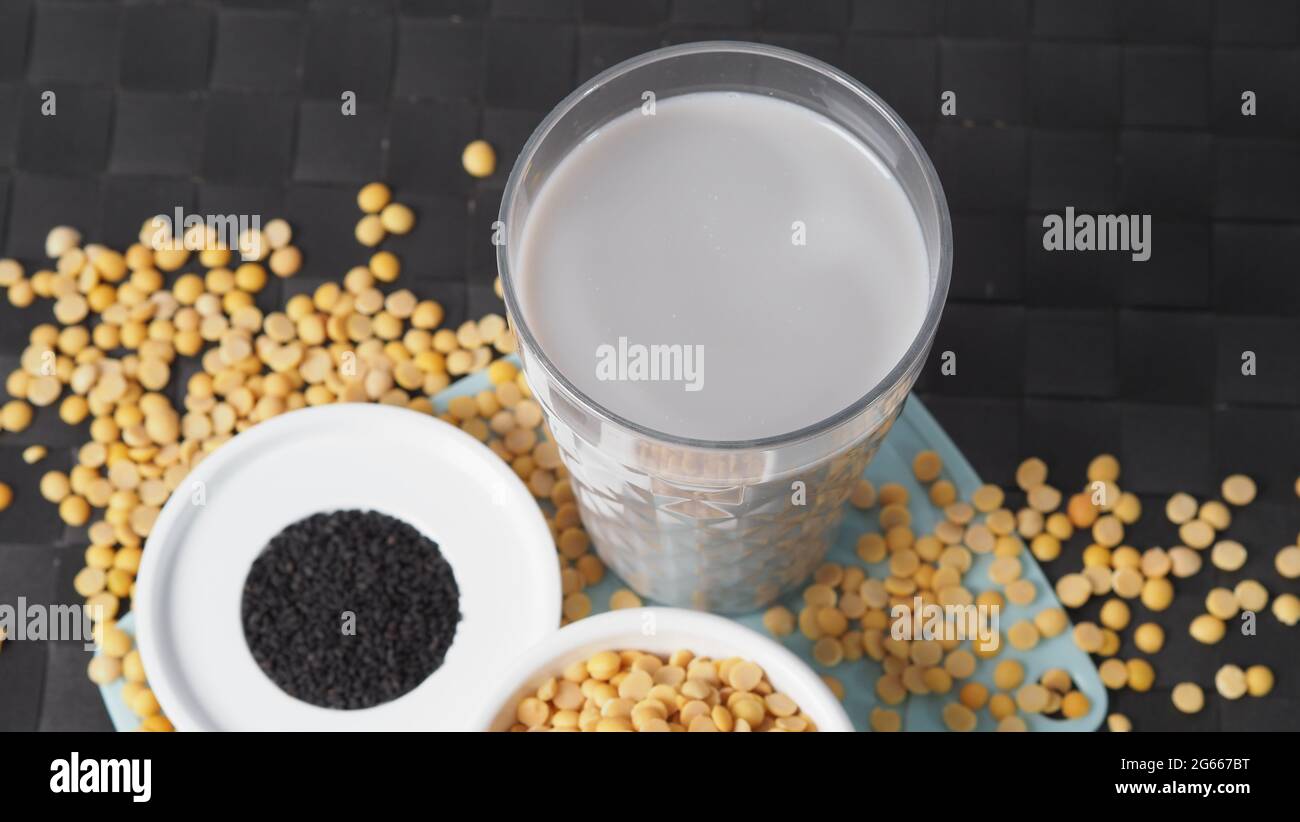 Soy milk blended with black sesame in clear glass on black plate mat ...