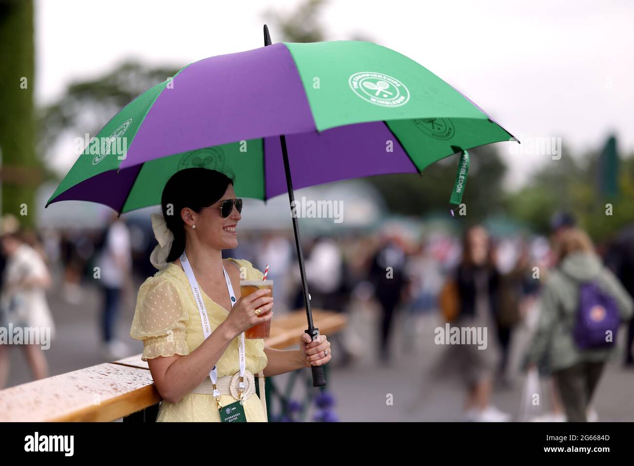 A spectator shelters from the rain under an official Wimbledon umbrella ...