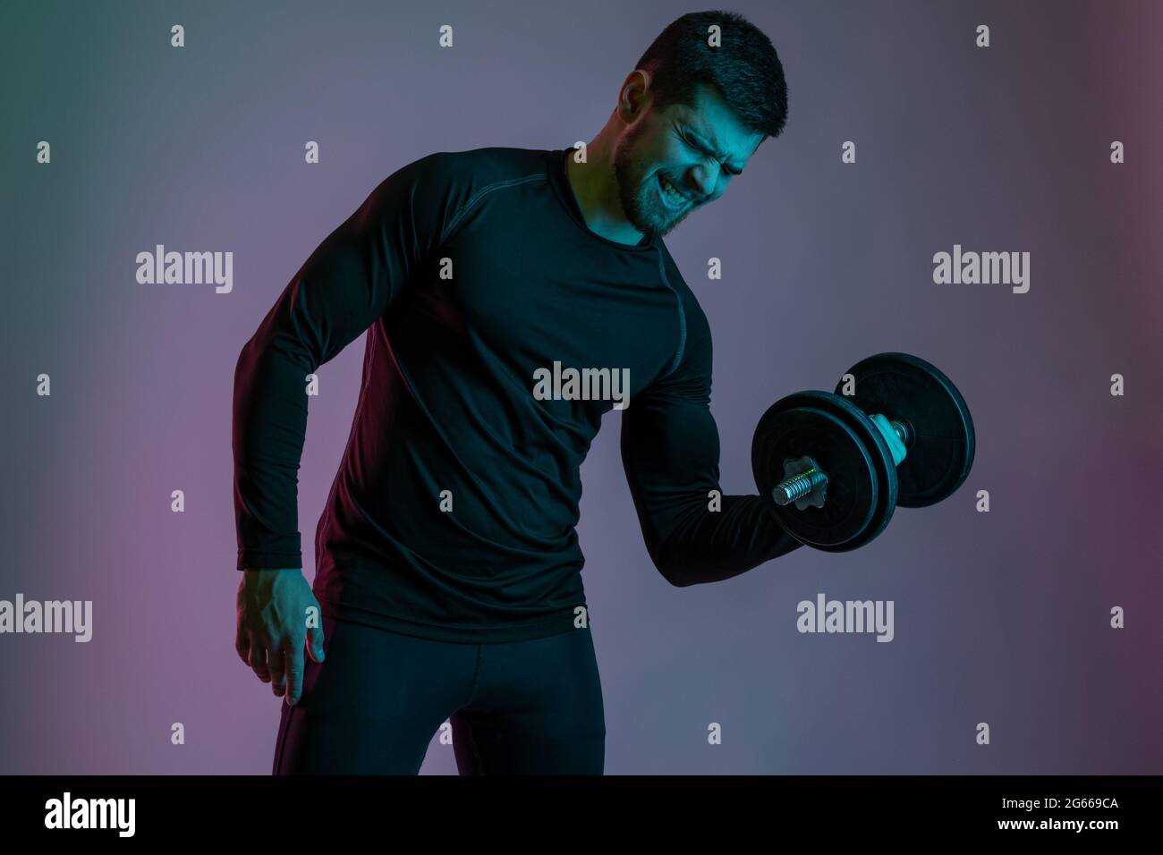 Emotional young bodybuilder performing bicep exercises with dumbbells ...