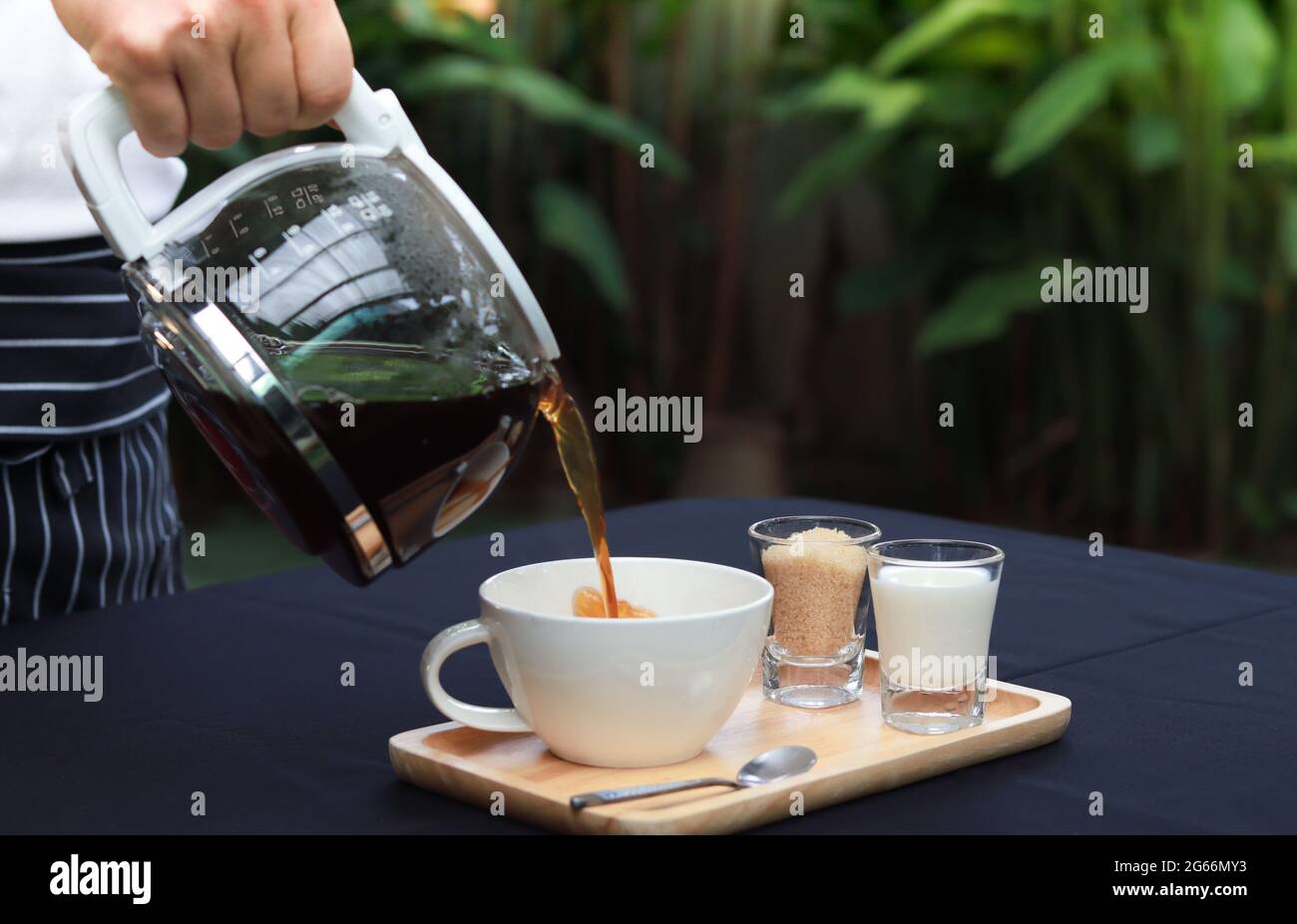 The waiter pouring coffee into cup. Coffee cup on wood tray with sugar ...