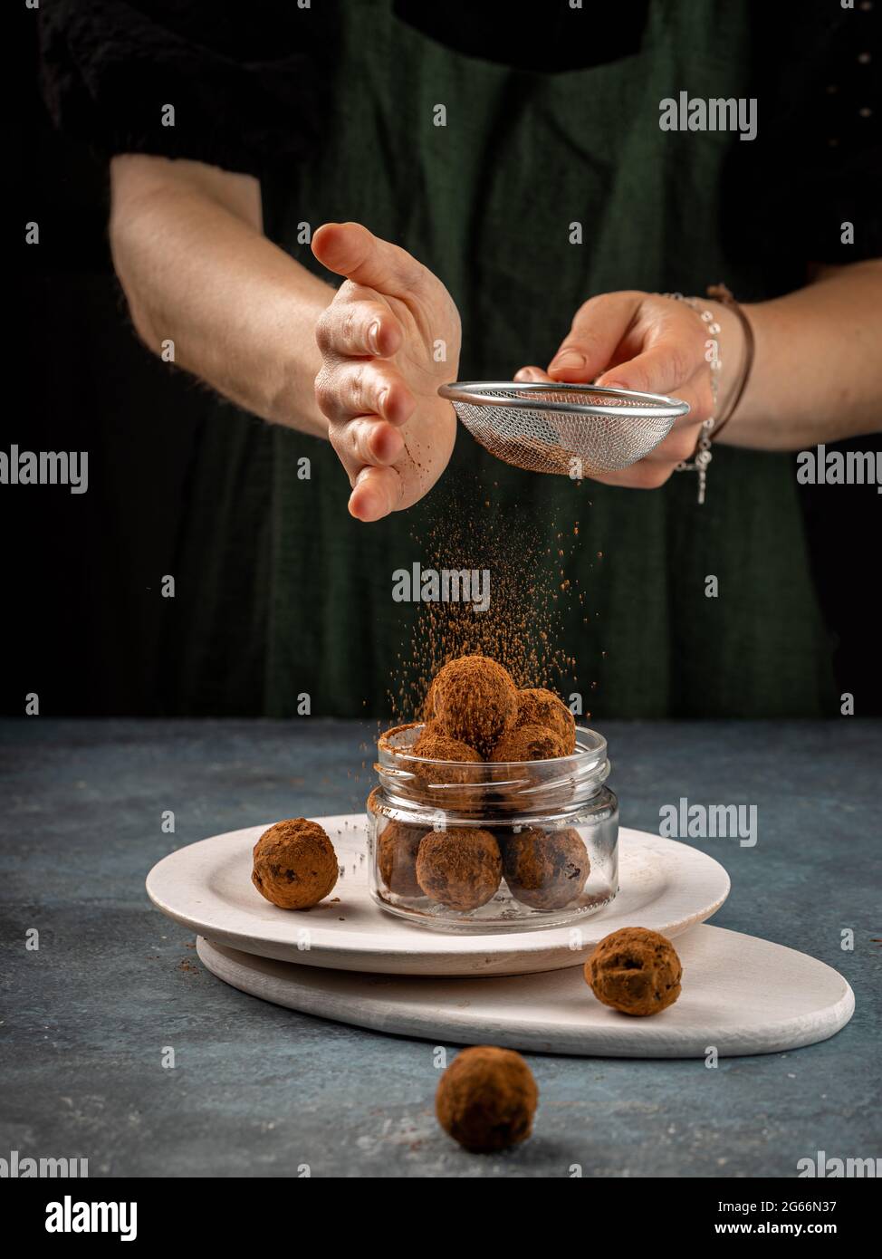 A woman sprinkle the chocolate balls with cocoa powder. Healthy kitchen ...