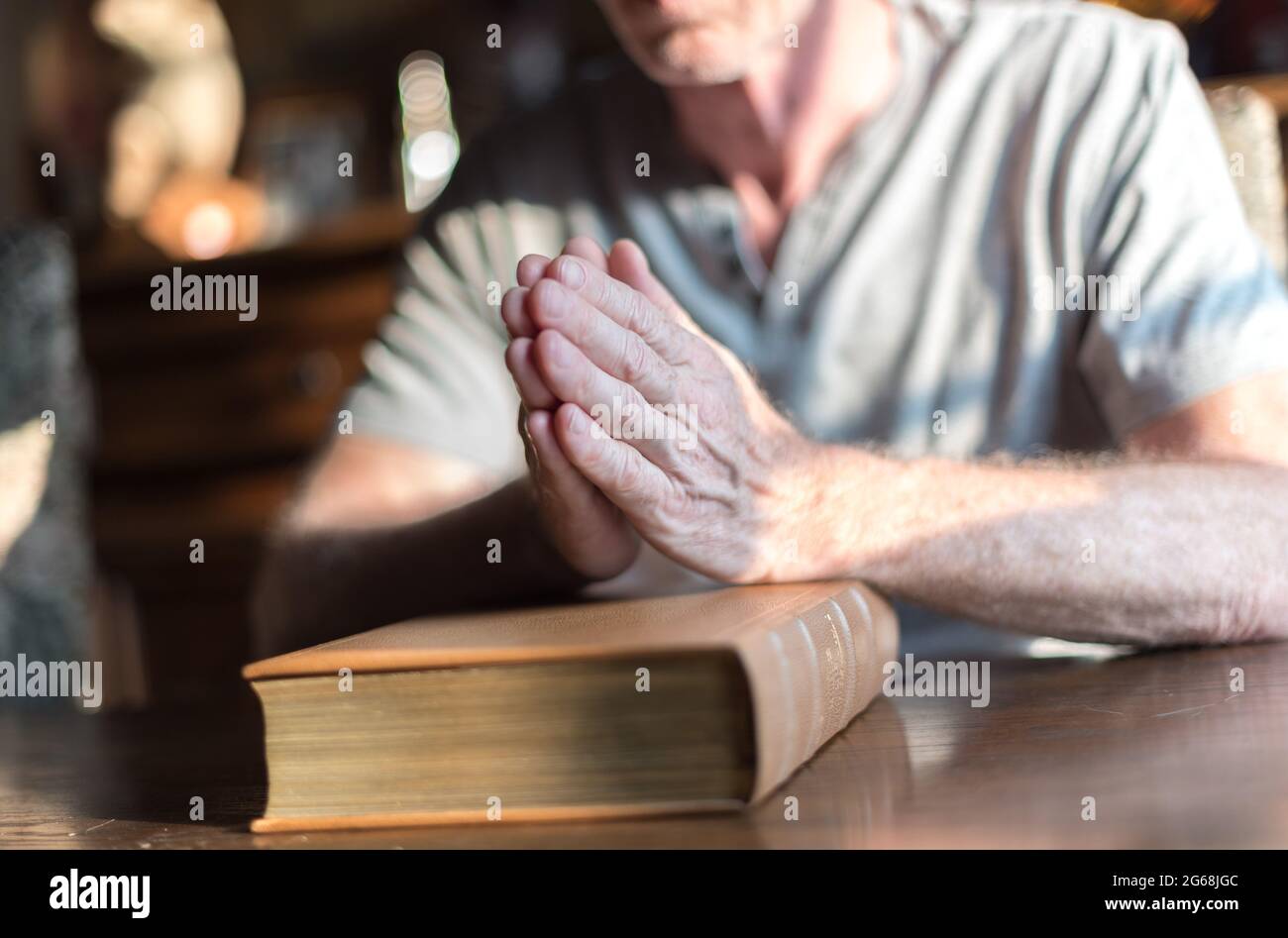 Man sitting at a table praying hands on a Bible Stock Photo - Alamy