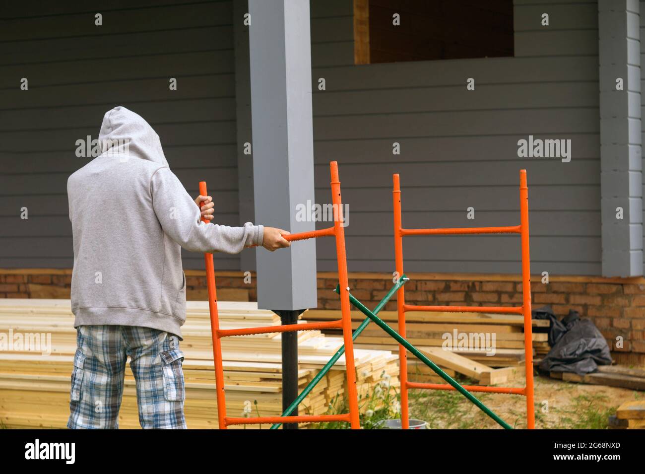 A worker in hood disassembling construction ladder or scaffolds ...