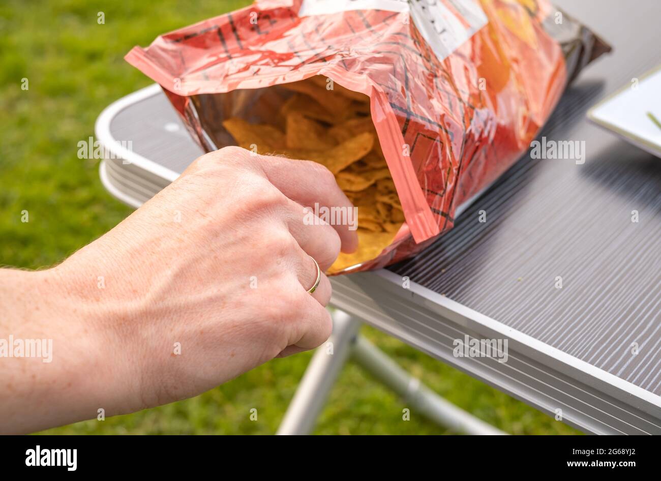 Unidentifiable human hand reaching in to a packet of sweet chilli ...