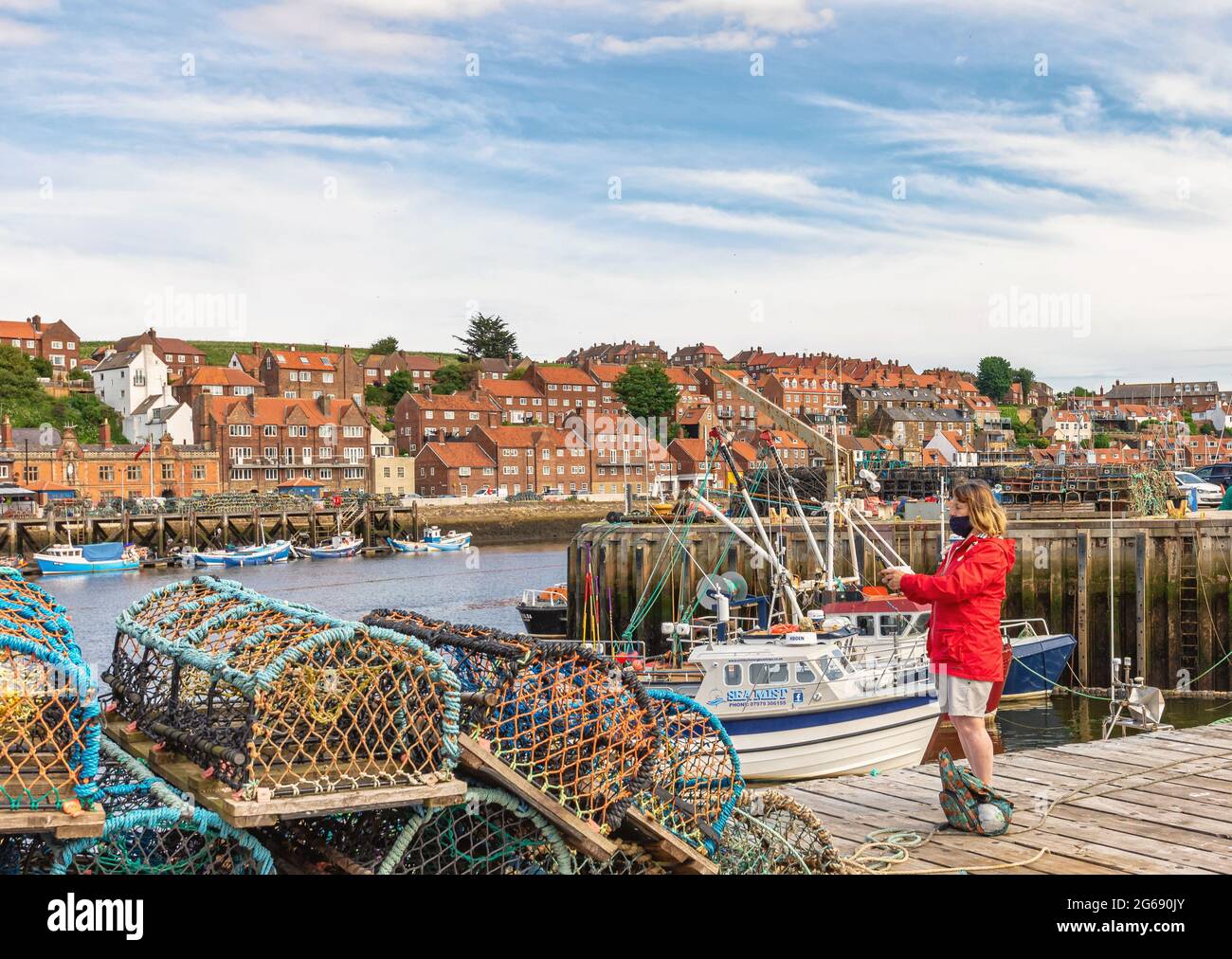 A woman, standing beside some lobster pots, takes a photograph with a ...