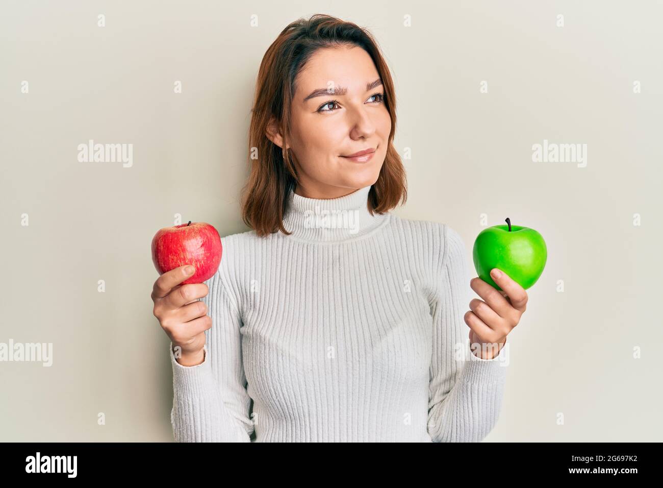 Young caucasian woman holding red and green apple smiling looking to ...