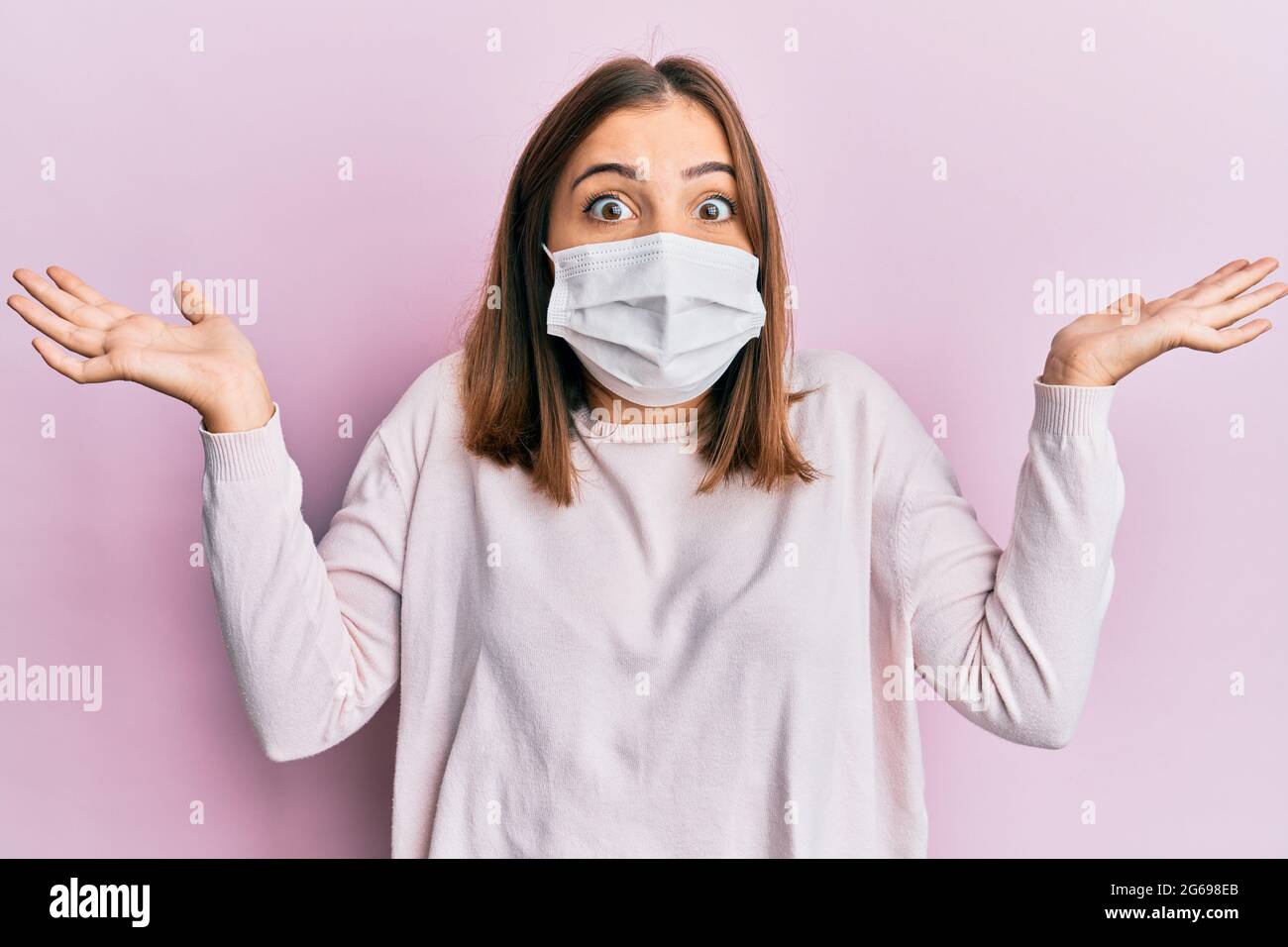 Young beautiful woman wearing medical mask clueless and confused with ...