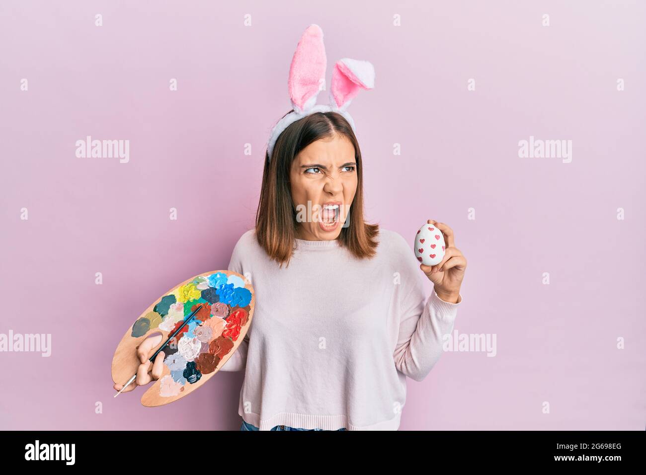 Young beautiful woman wearing cute easter bunny ears holding painting ...