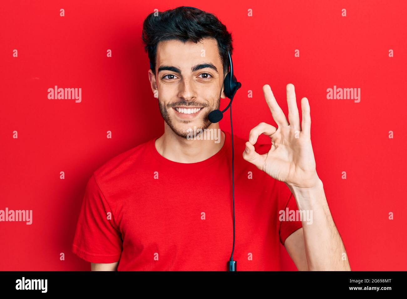 Young hispanic man wearing call center agent headset doing ok sign with ...