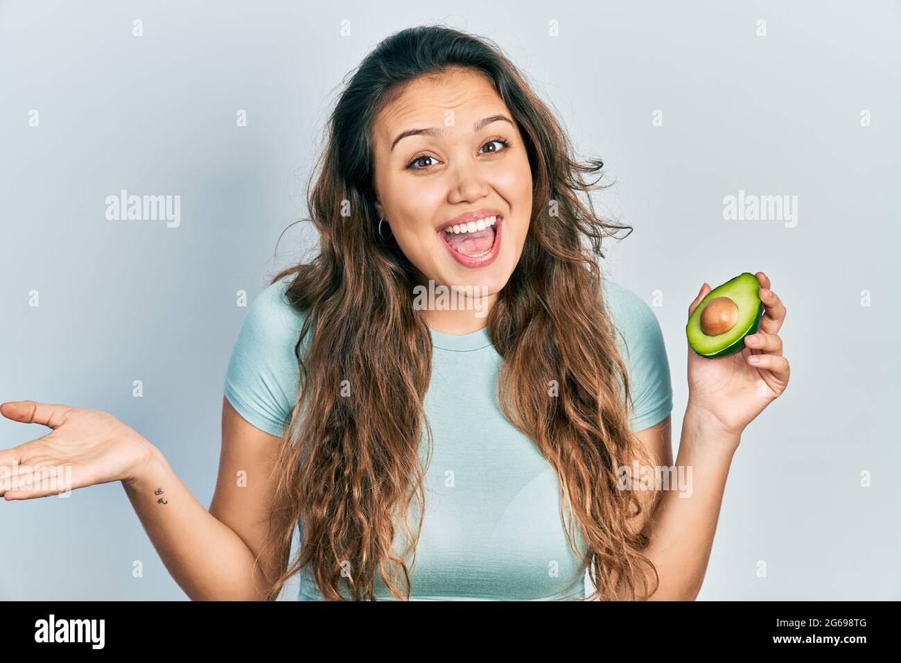 Young hispanic girl holding middle avocado celebrating achievement with ...