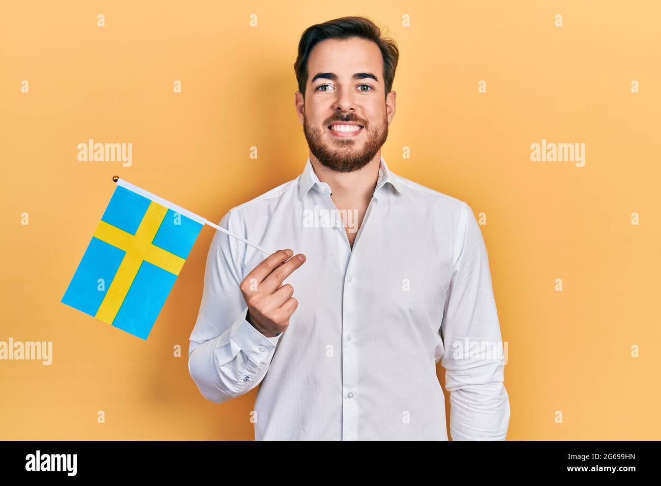 Handsome caucasian man with beard holding sweden flag looking positive ...