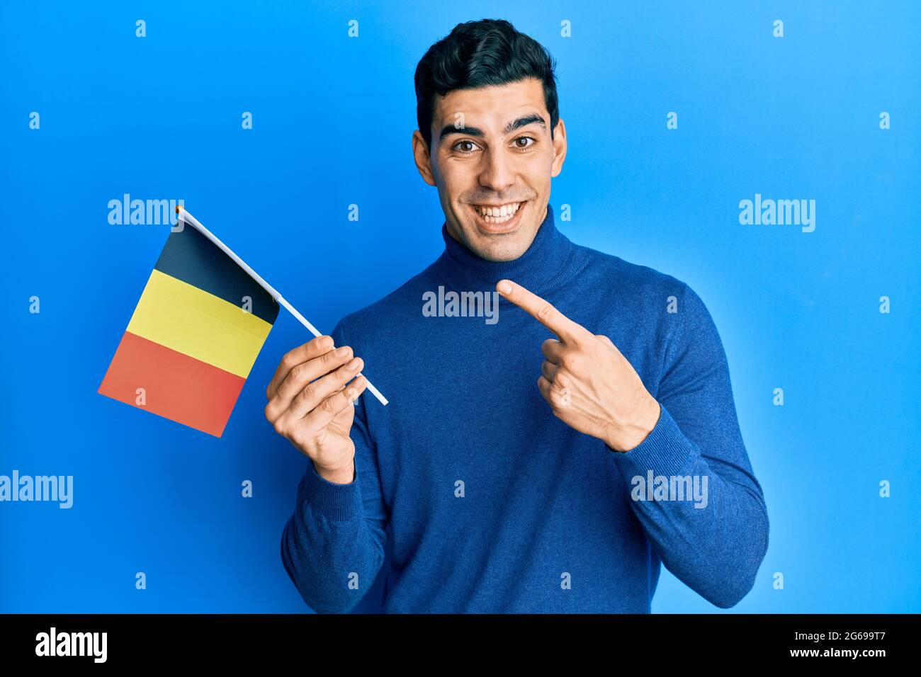 Handsome hispanic man holding belgium flag smiling happy pointing with ...