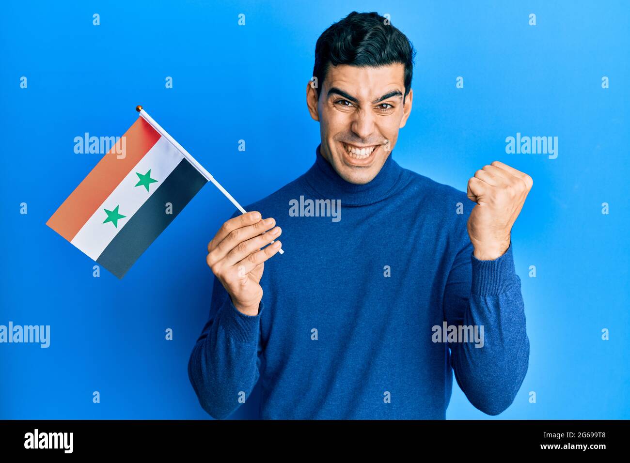 Handsome hispanic man holding syria flag screaming proud, celebrating ...