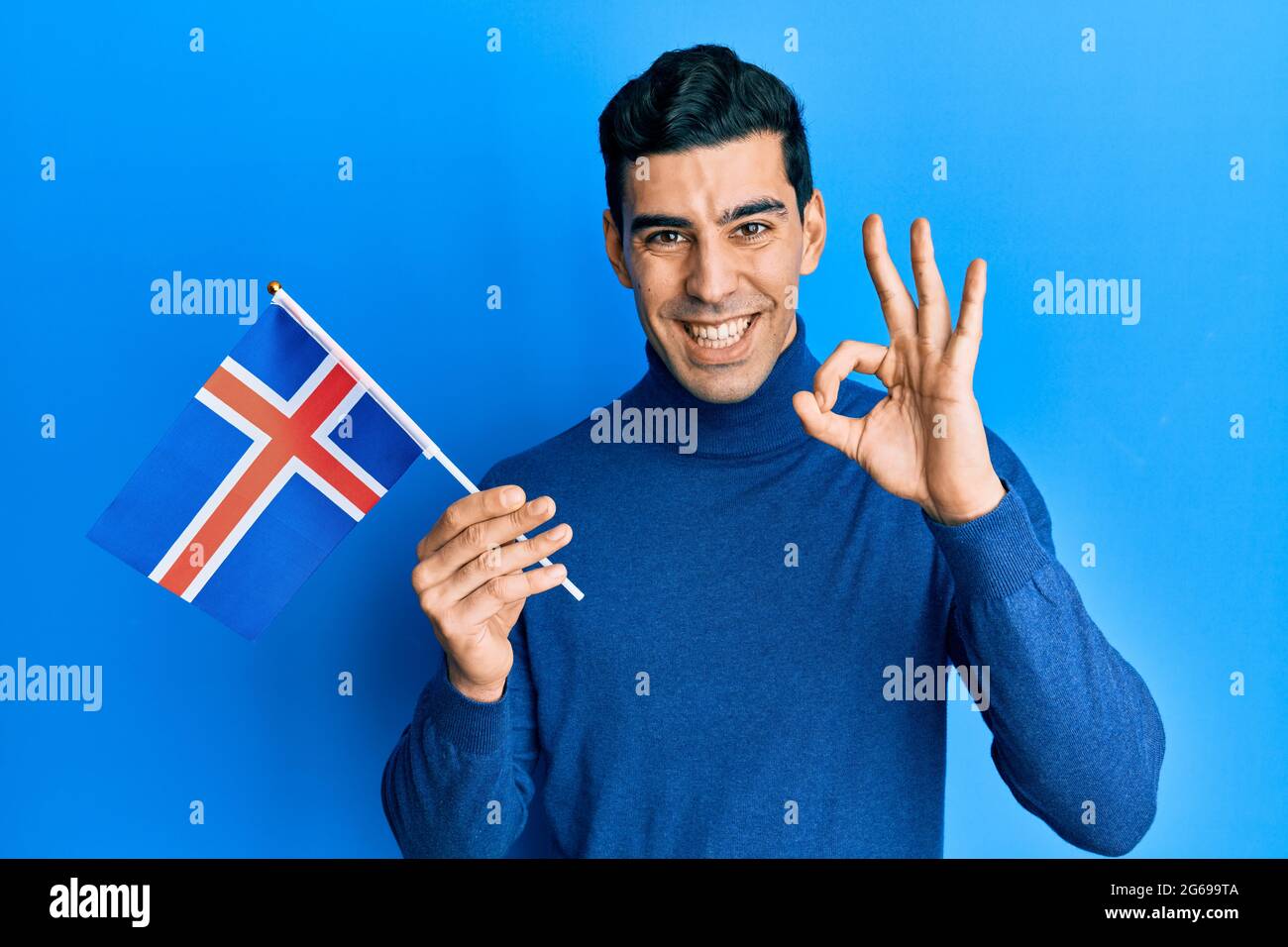 Handsome hispanic man holding island flag doing ok sign with fingers ...