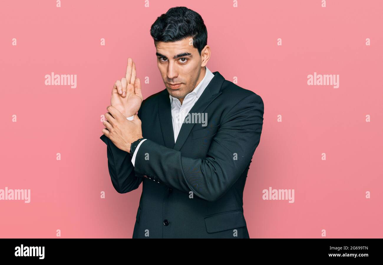 Handsome hispanic man wearing business clothes holding symbolic gun ...