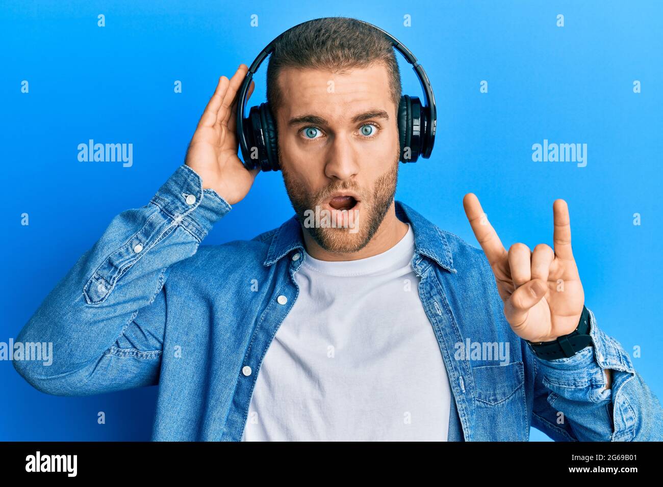 Young caucasian man using headphones and doing rock symbol in shock ...