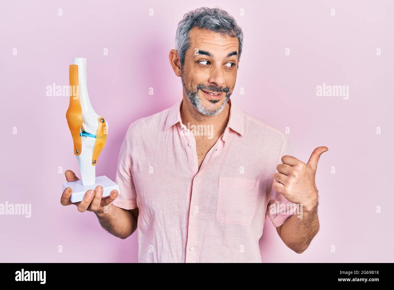 Handsome middle age man with grey hair holding anatomical model of knee ...