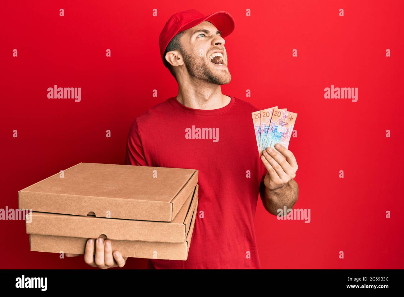 Young caucasian man holding delivery box and swiss franc banknotes ...