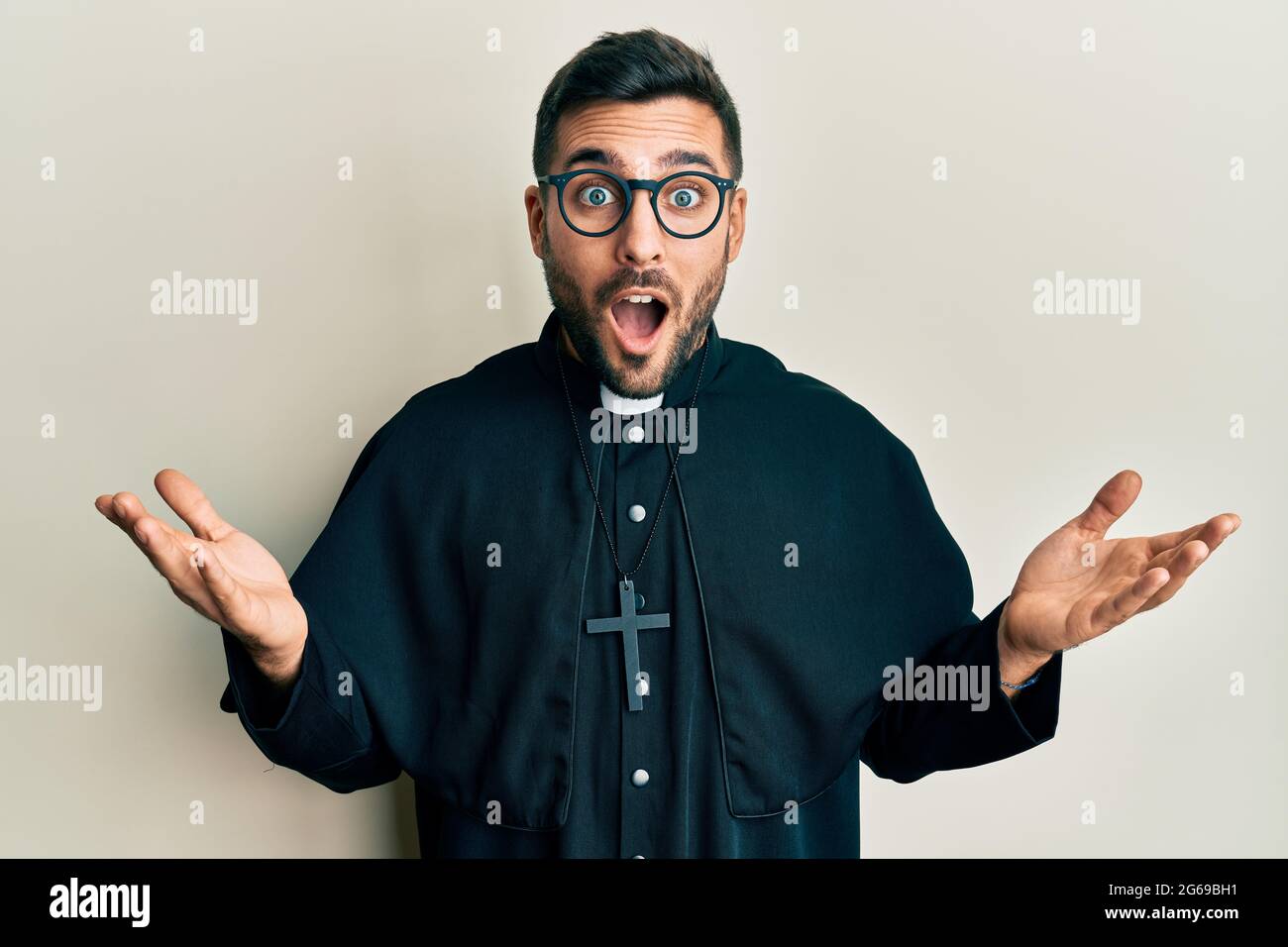 Young hispanic priest man standing over white background afraid and ...
