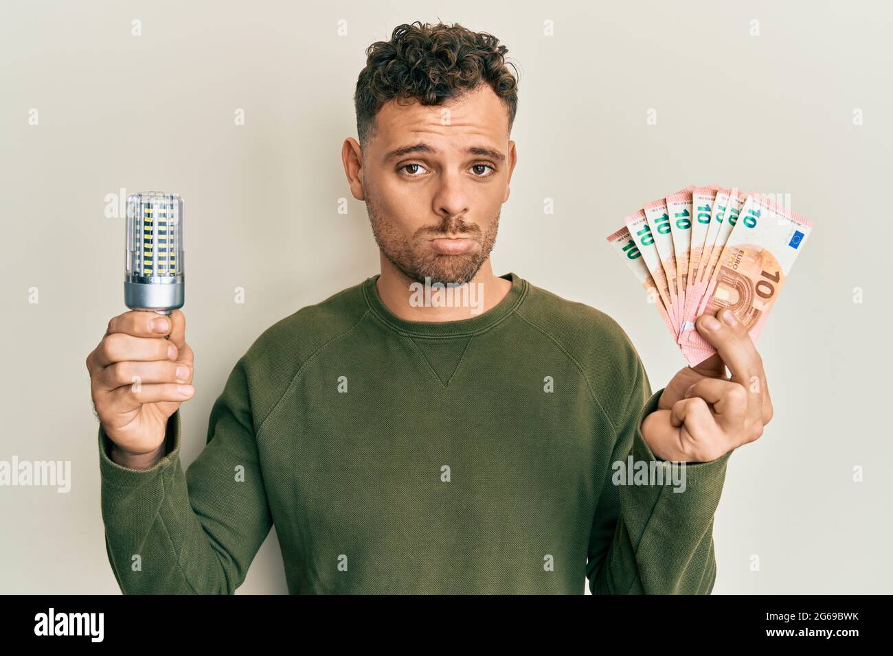 Young hispanic man holding led bulb and euros banknotes depressed and ...