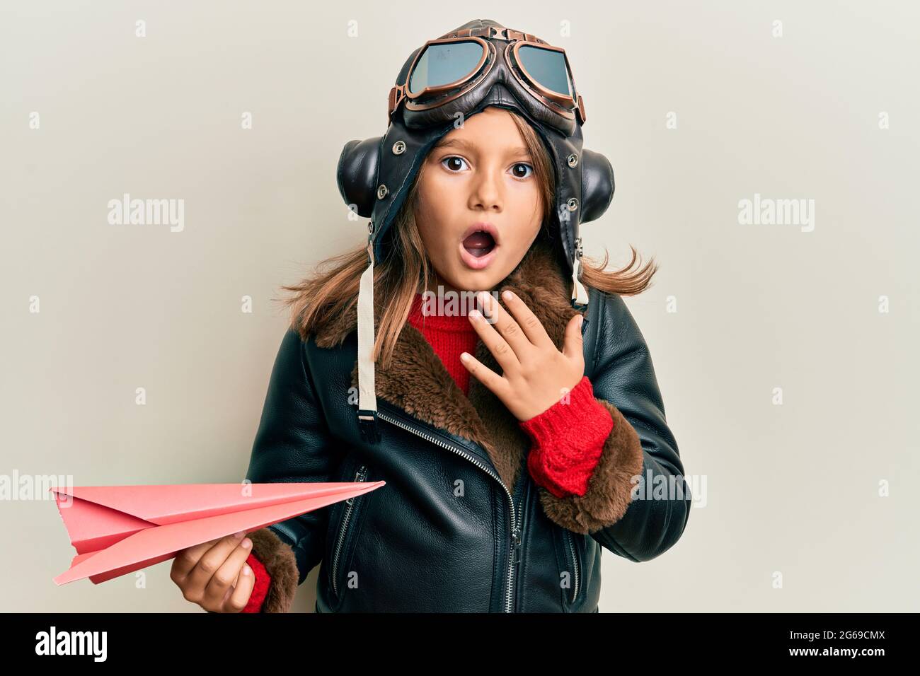 Little beautiful girl wearing pilot uniform holding paper plane scared ...