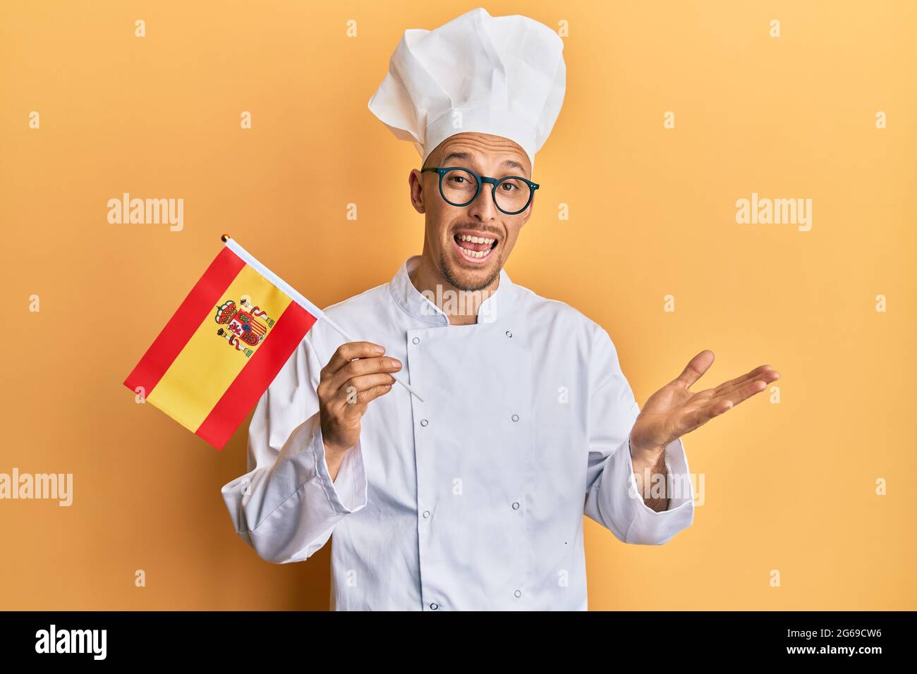Bald man with beard wearing professional cook apron holding spanish ...