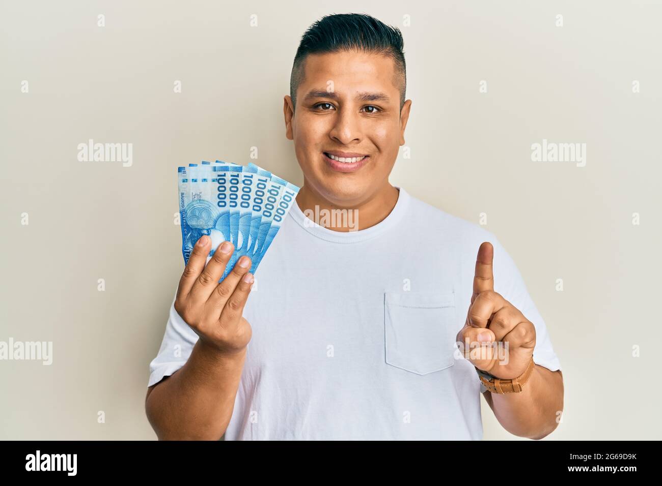 Young latin man holding 10000 chilean pesos smiling with an idea or ...