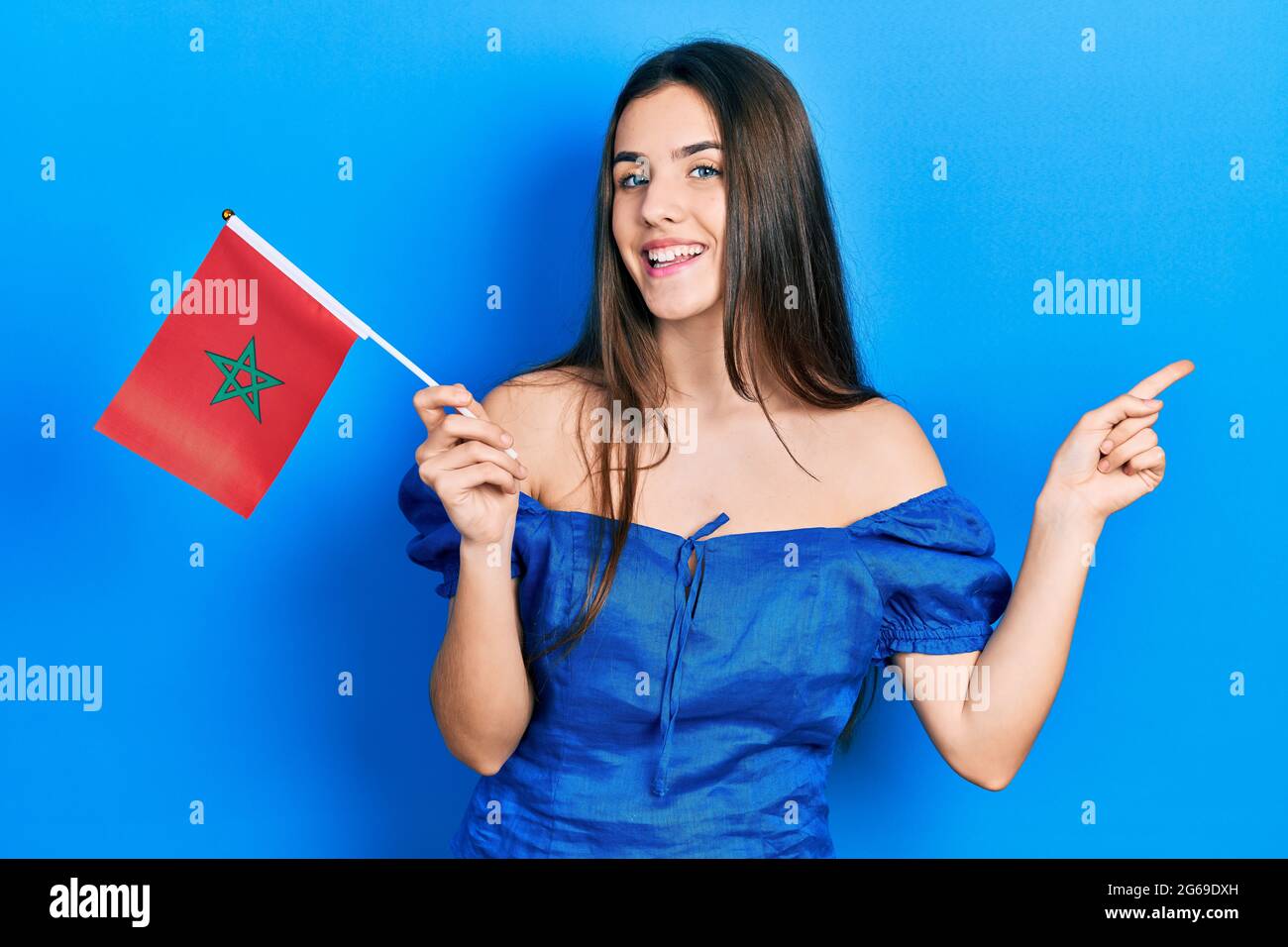 Young brunette teenager holding morocco flag smiling happy pointing ...